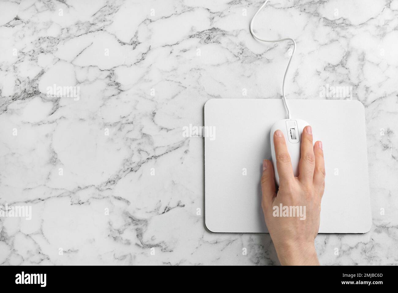 Woman using modern wired optical mouse on white marble table, top view ...