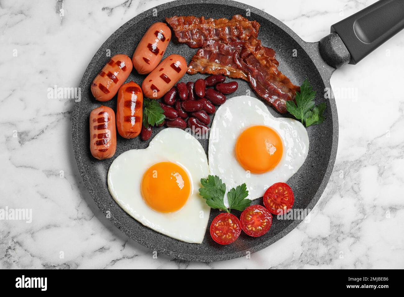 Delicious breakfast with heart shaped fried eggs and sausages on white marble table, top view ...