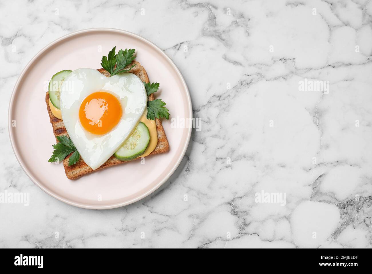 Plate of tasty sandwich with heart shaped fried egg on white marble table, top view. Space for ...