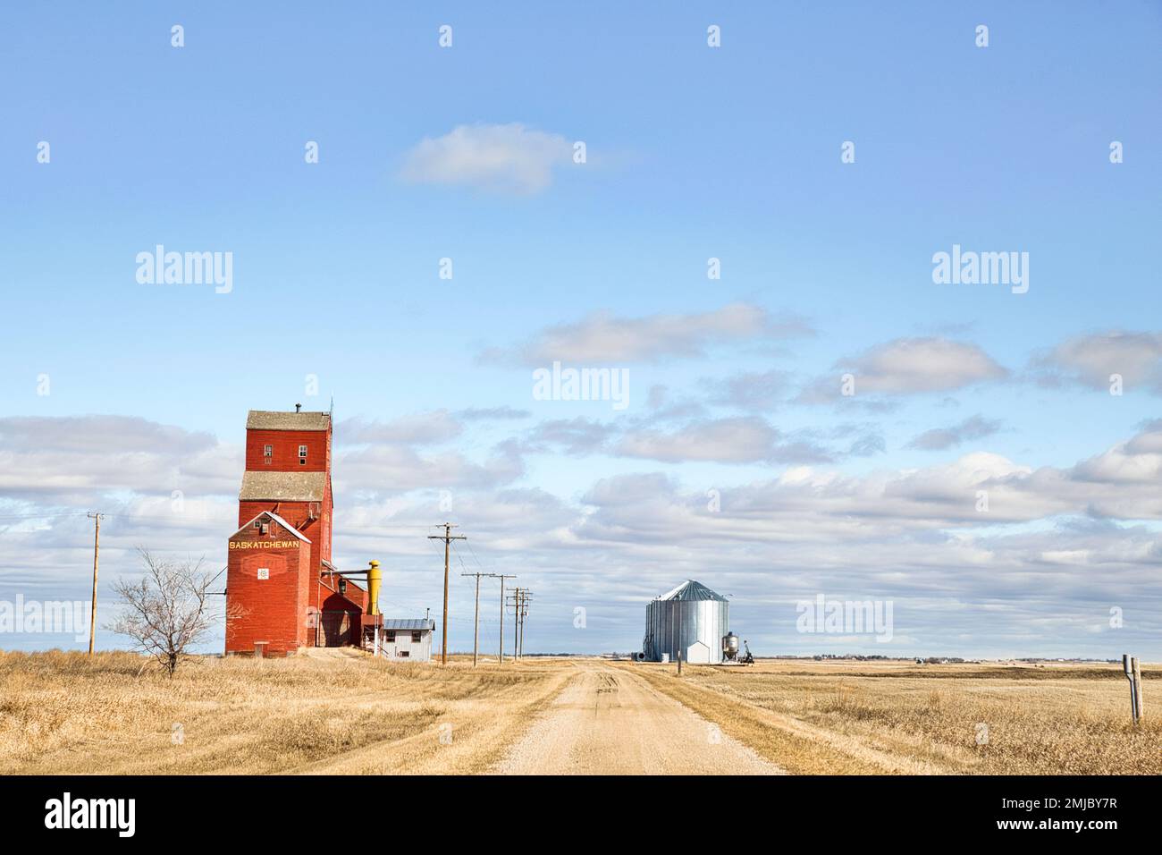 A gravel road cutting between an old red wooden grain elevatpr and ...