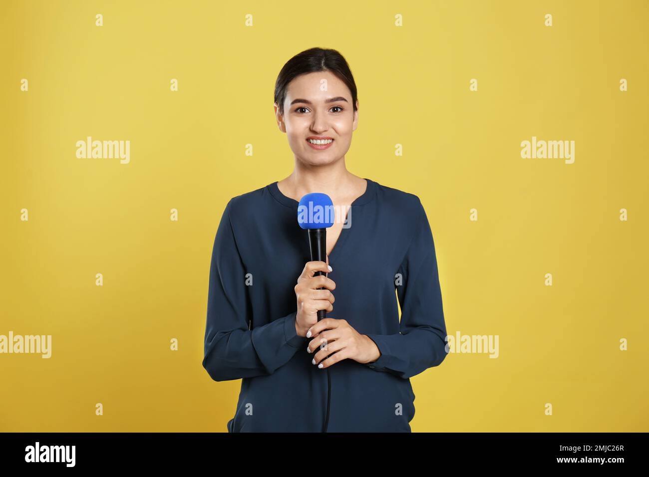 Young female journalist with microphone on yellow background Stock ...