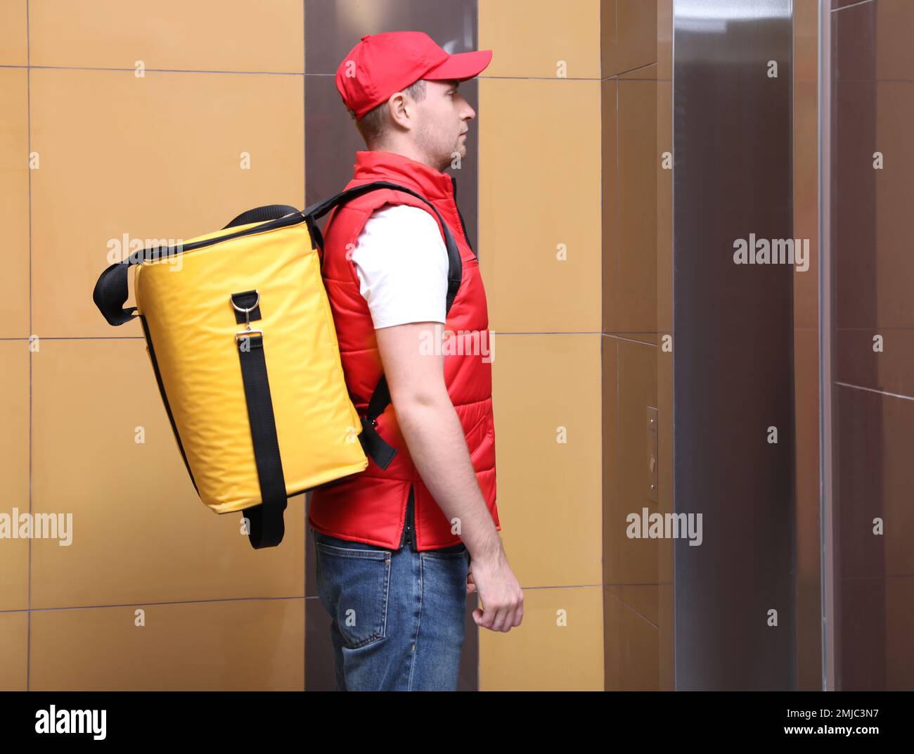 Male courier with thermo bag waiting for elevator. Food delivery ...