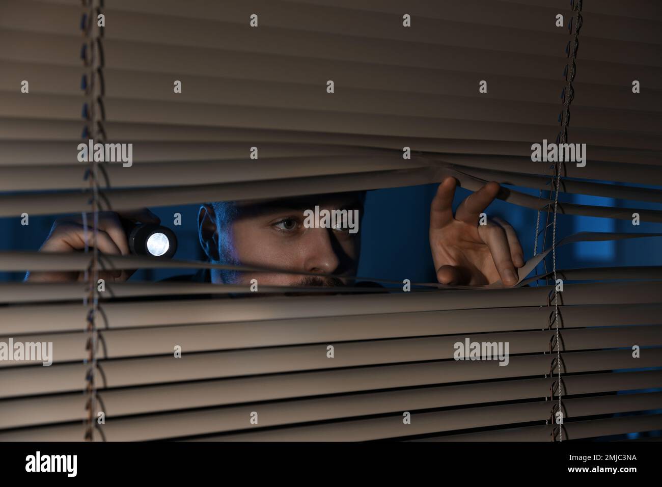 Male security guard with flashlight looking through window blinds in ...
