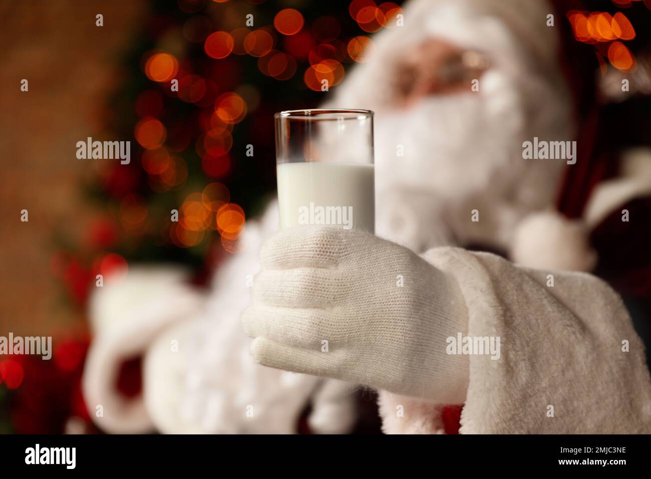 Santa Claus holding glass of milk against blurred Christmas lights ...