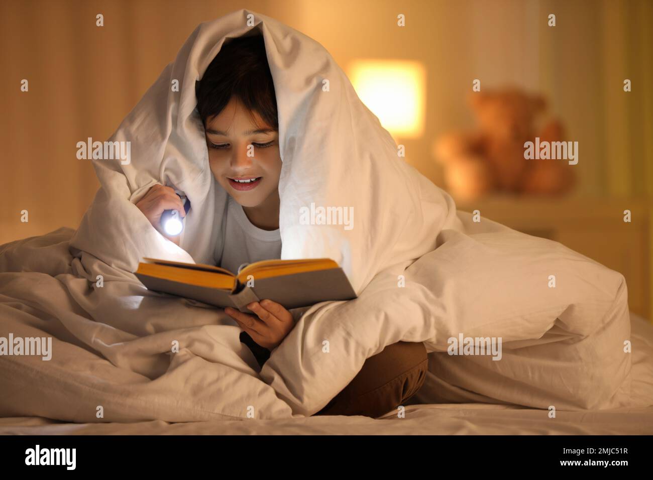 Boy with flashlight reading book under blanket at home Stock Photo - Alamy