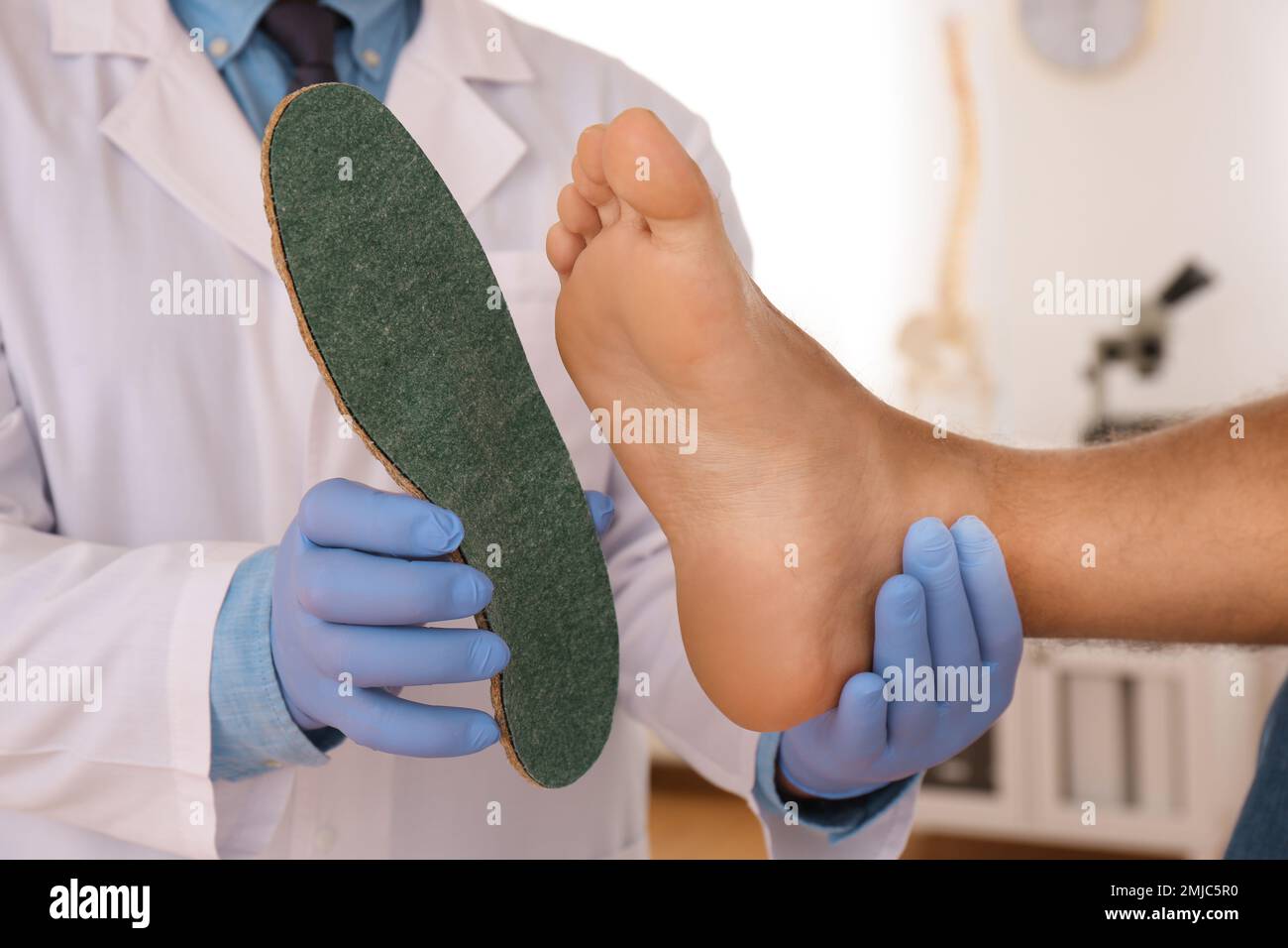Male orthopedist fitting insole on patient's foot in clinic, closeup ...