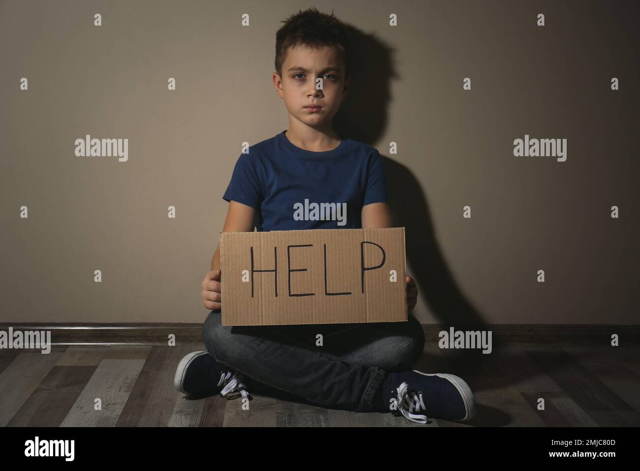 Abused little boy with sign HELP near beige wall. Domestic violence ...