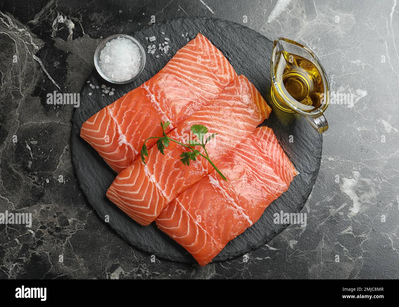 Top view of fresh raw salmon with parsley, oil and salt on black marble ...