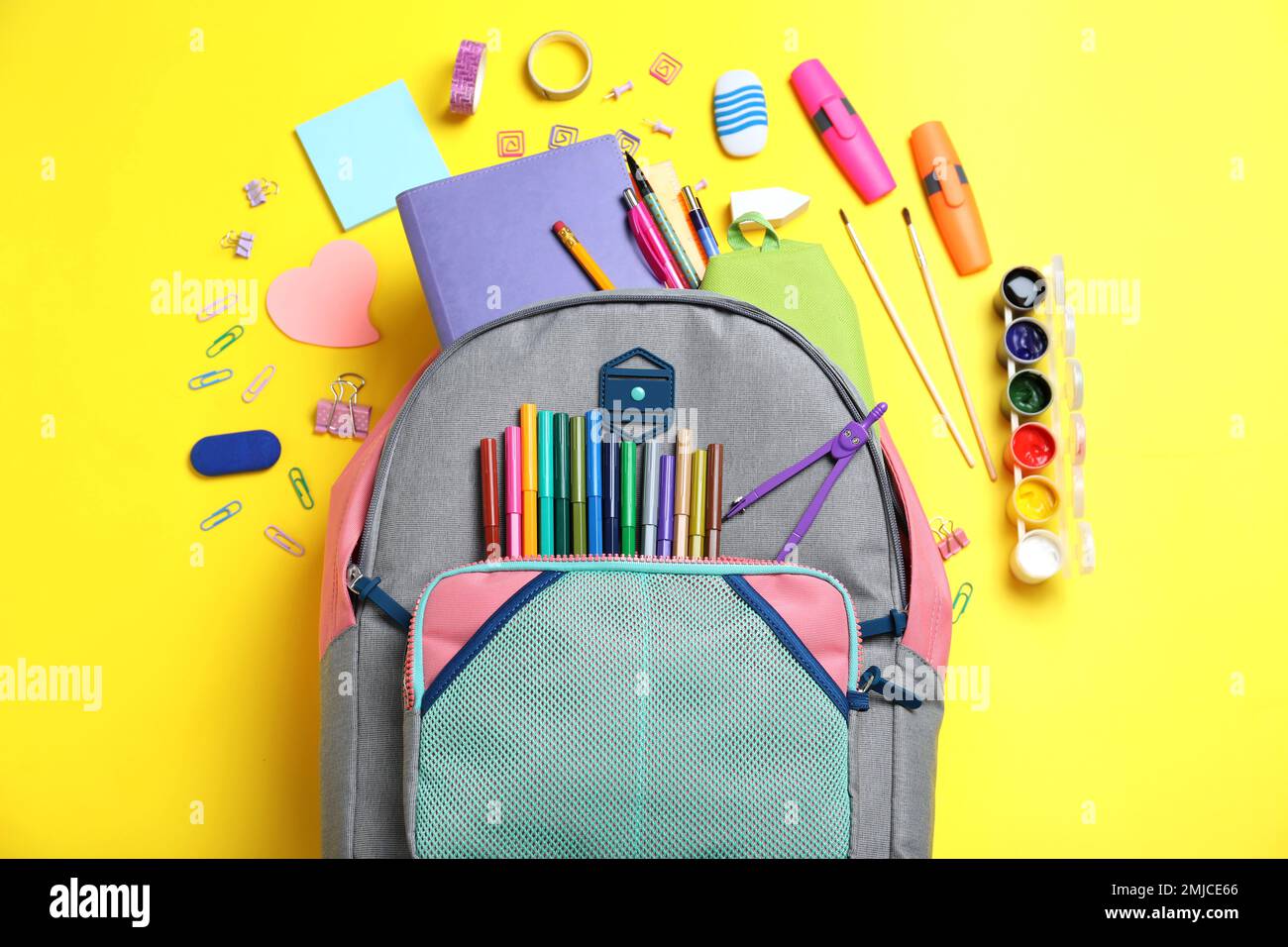 Stylish backpack with different school stationery on yellow background ...