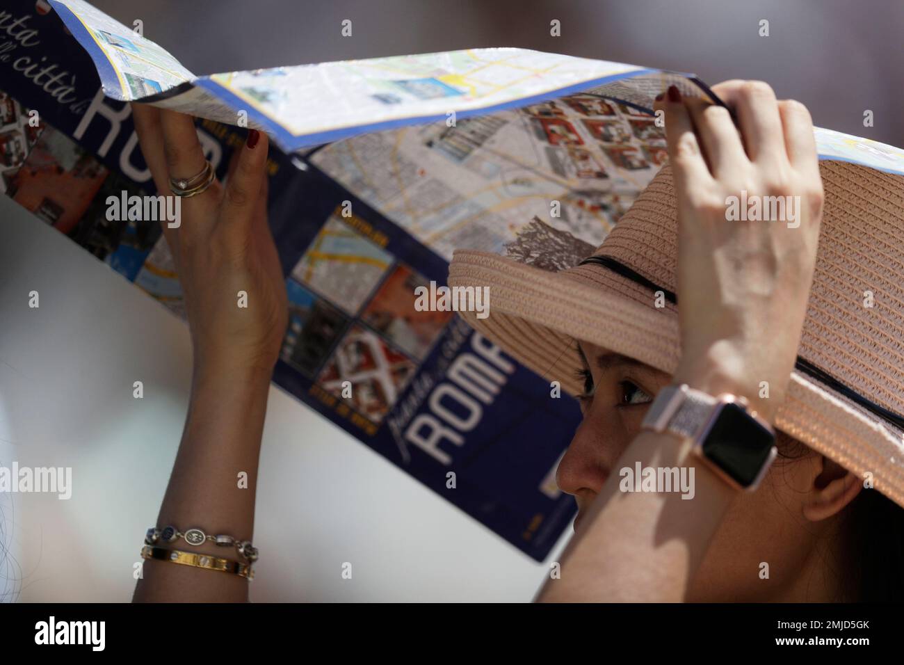 A woman uses a map of Rome to shade herself from the sun during Pope ...