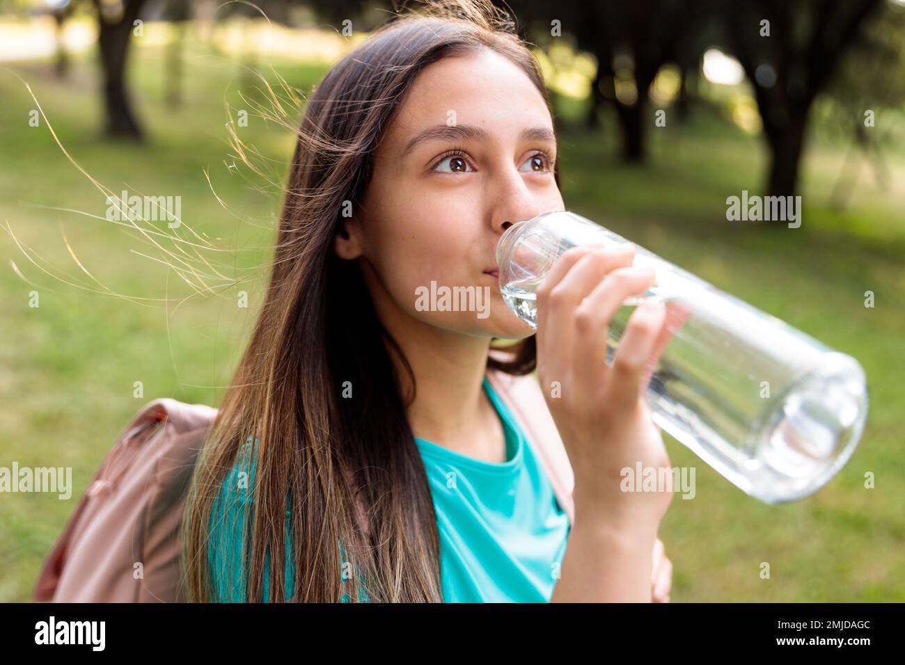 Young caucasian girl drinking water from a glass bottle at the park ...