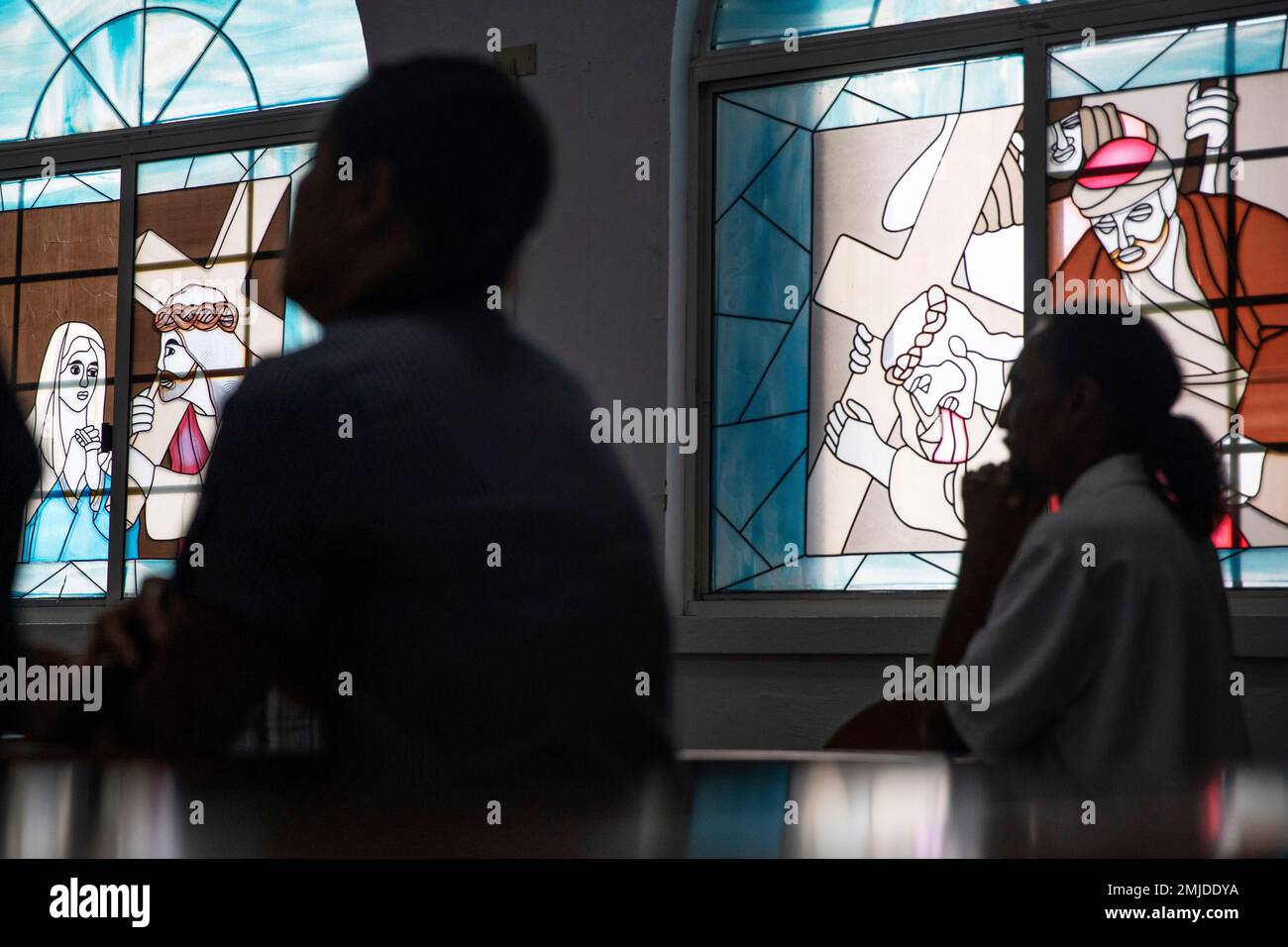 Parishioners are silhouetted by stained glass windows while praying at ...