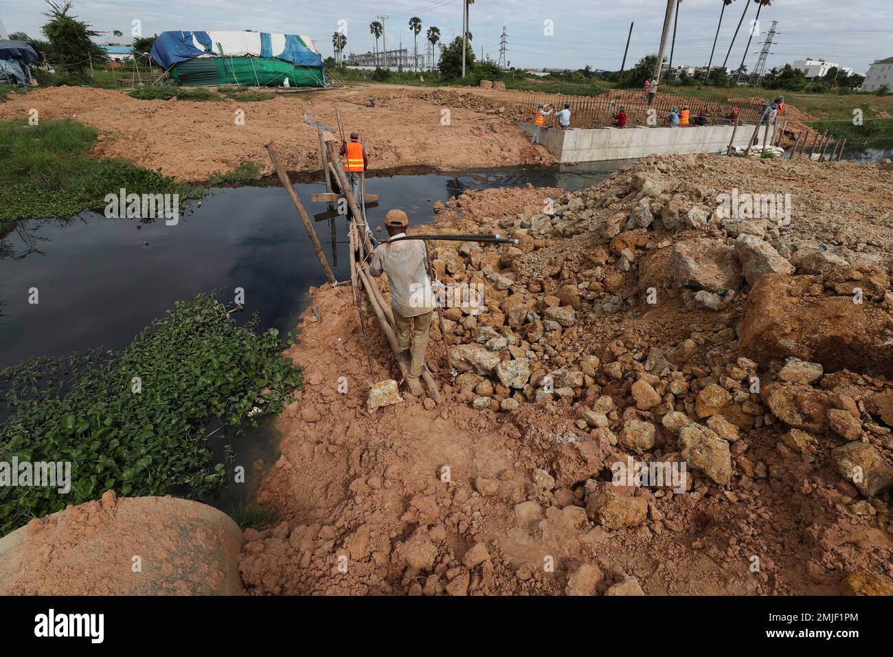 Workers carry construction steels through a wooden bridge where they ...