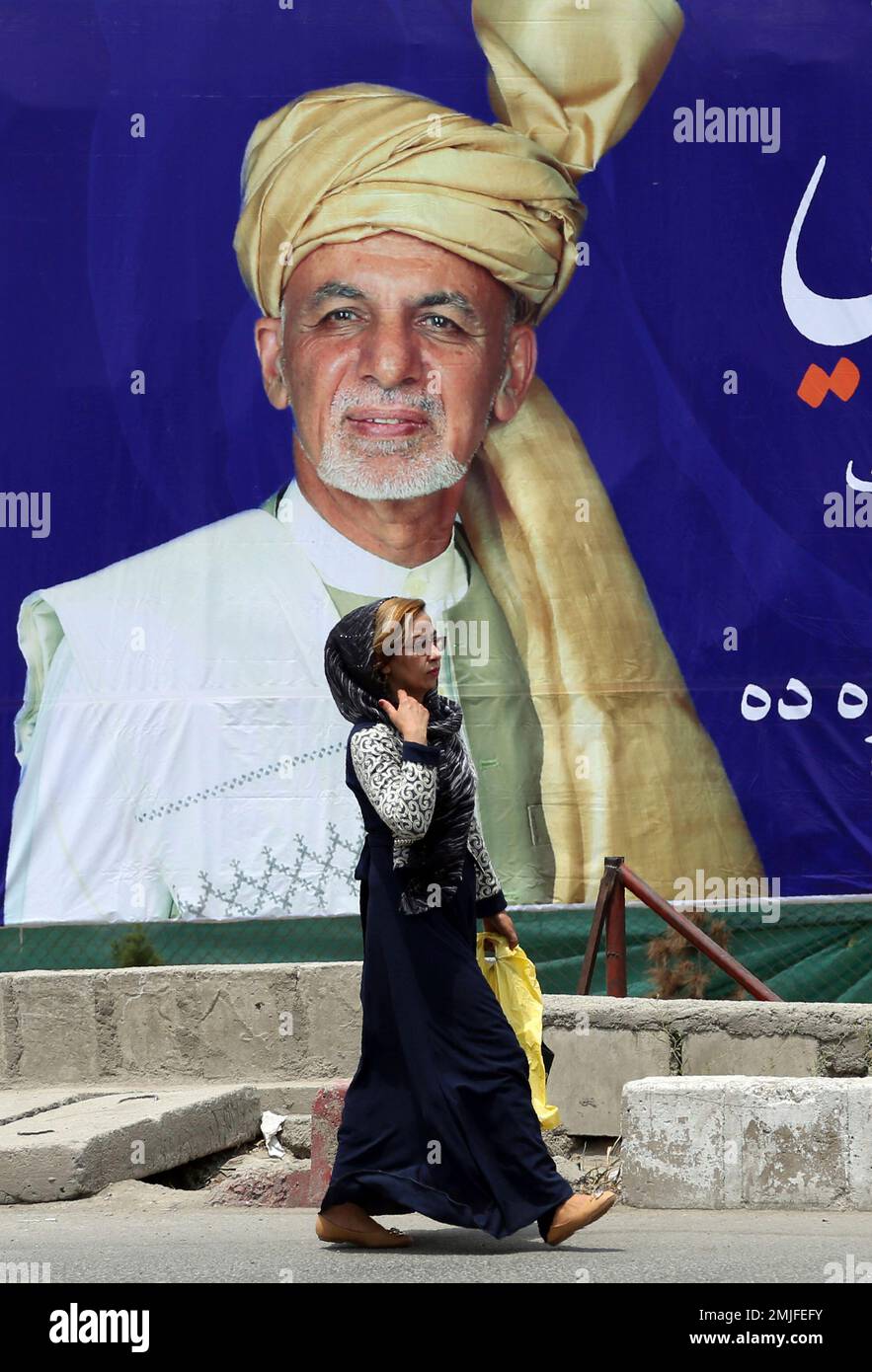 An Afghan woman walks past an election poster of presidential candidate ...