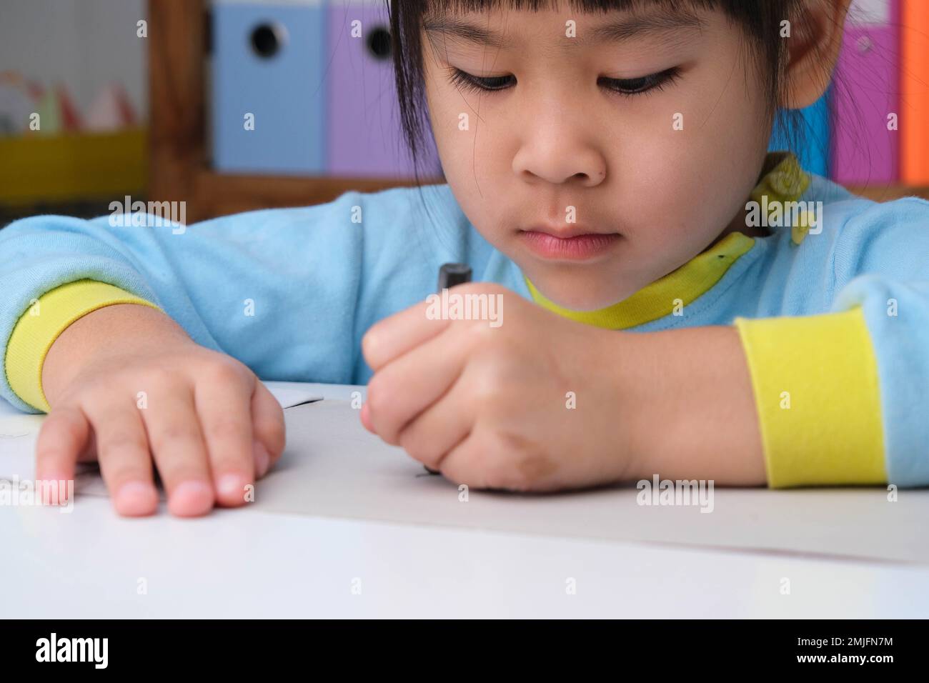 Cheerful happy little girl drawing with crayons on paper sitting at ...
