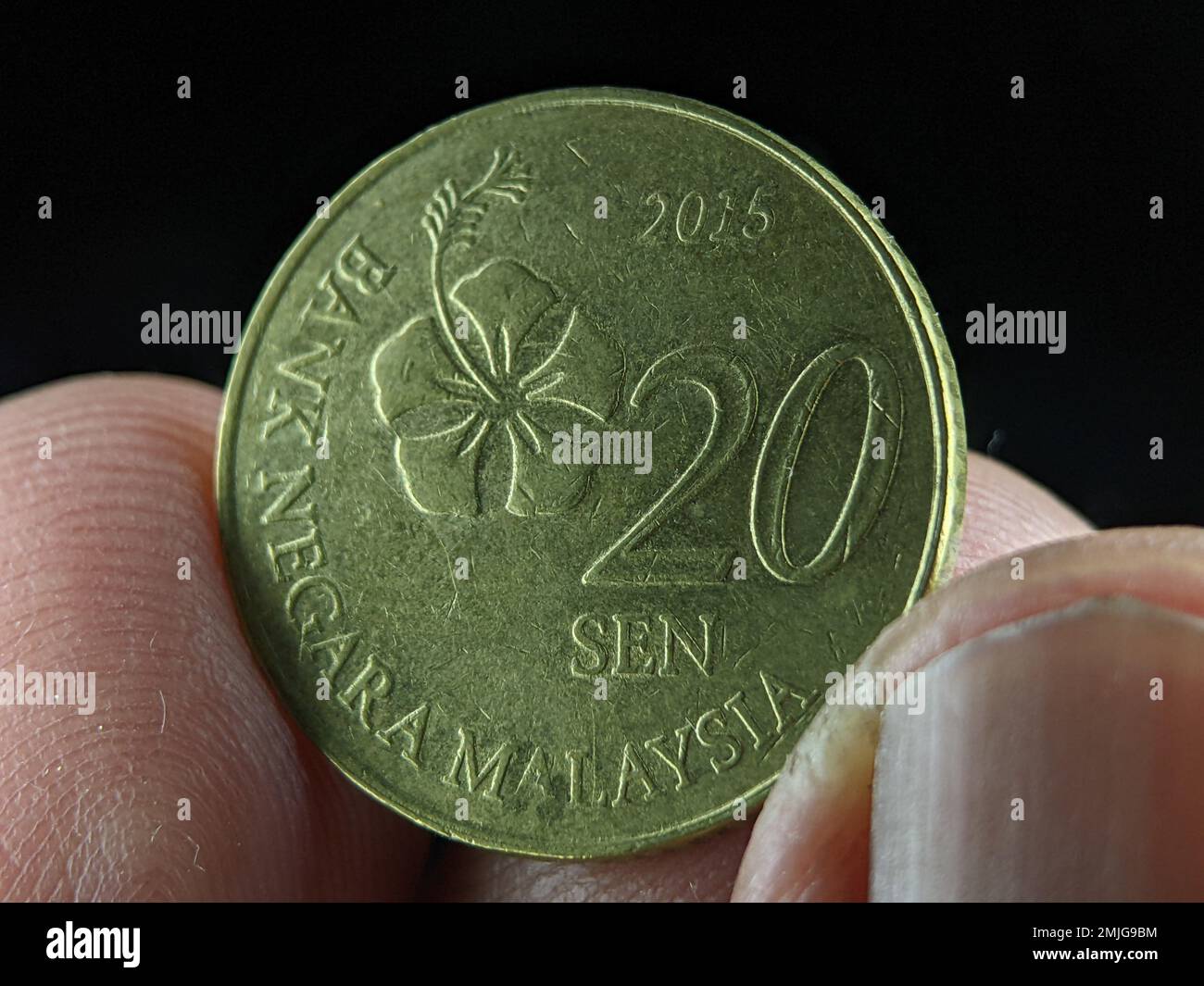 Closeup finger holding 20 cent Malaysia coin on a black background ...