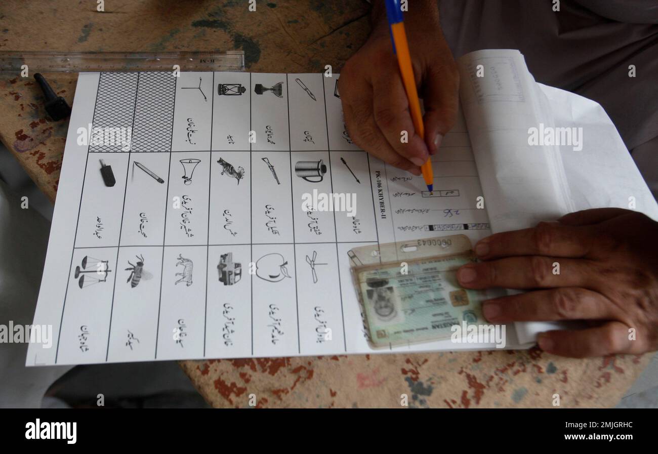 An election worker prepares ballot paper for a tribesman, waiting to ...