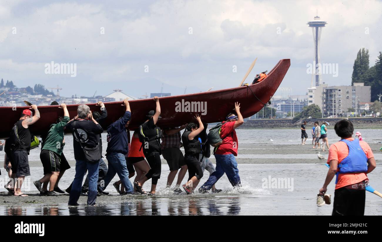 Canoe pullers and volunteers heft a canoe in view of the Space Needle ...