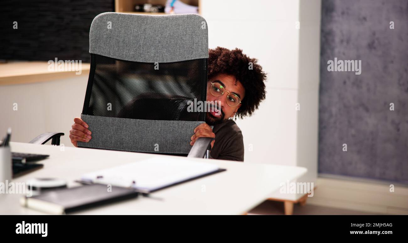Scared Man Hiding Behind Office Desk In Room Stock Photo - Alamy