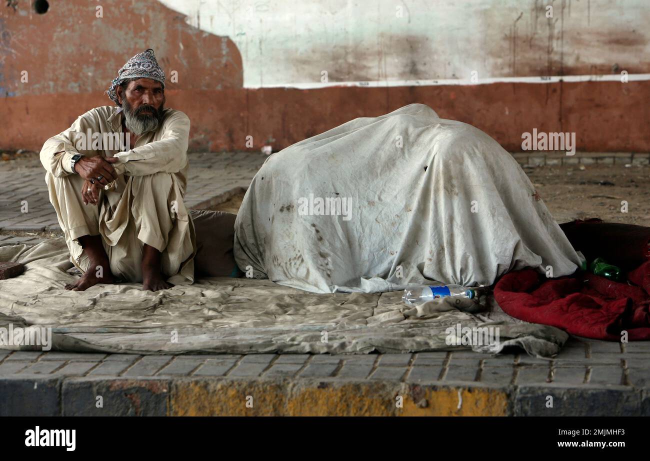 A Pakistani drug addict sits next to his friend under a sheet at a ...