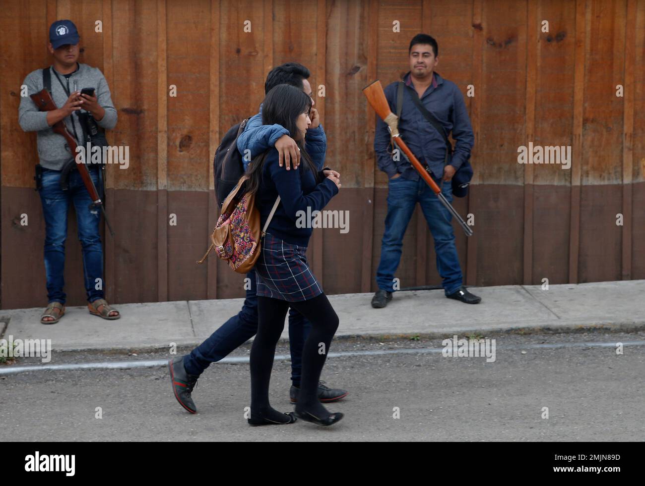 Students walk home past FUPCEG vigilantes standing guard along a ...