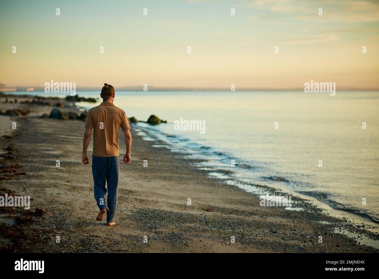 Nothing calms the mind like a walk on the beach. Rearview shot of a man ...