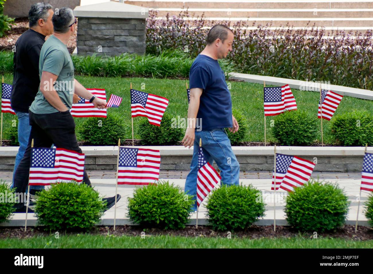 A group of men walks through the American flags lining sidewalks around ...