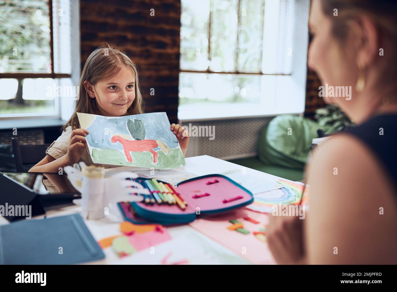 Girl presenting her artwork teacher. Woman assisting schoolgirl during ...