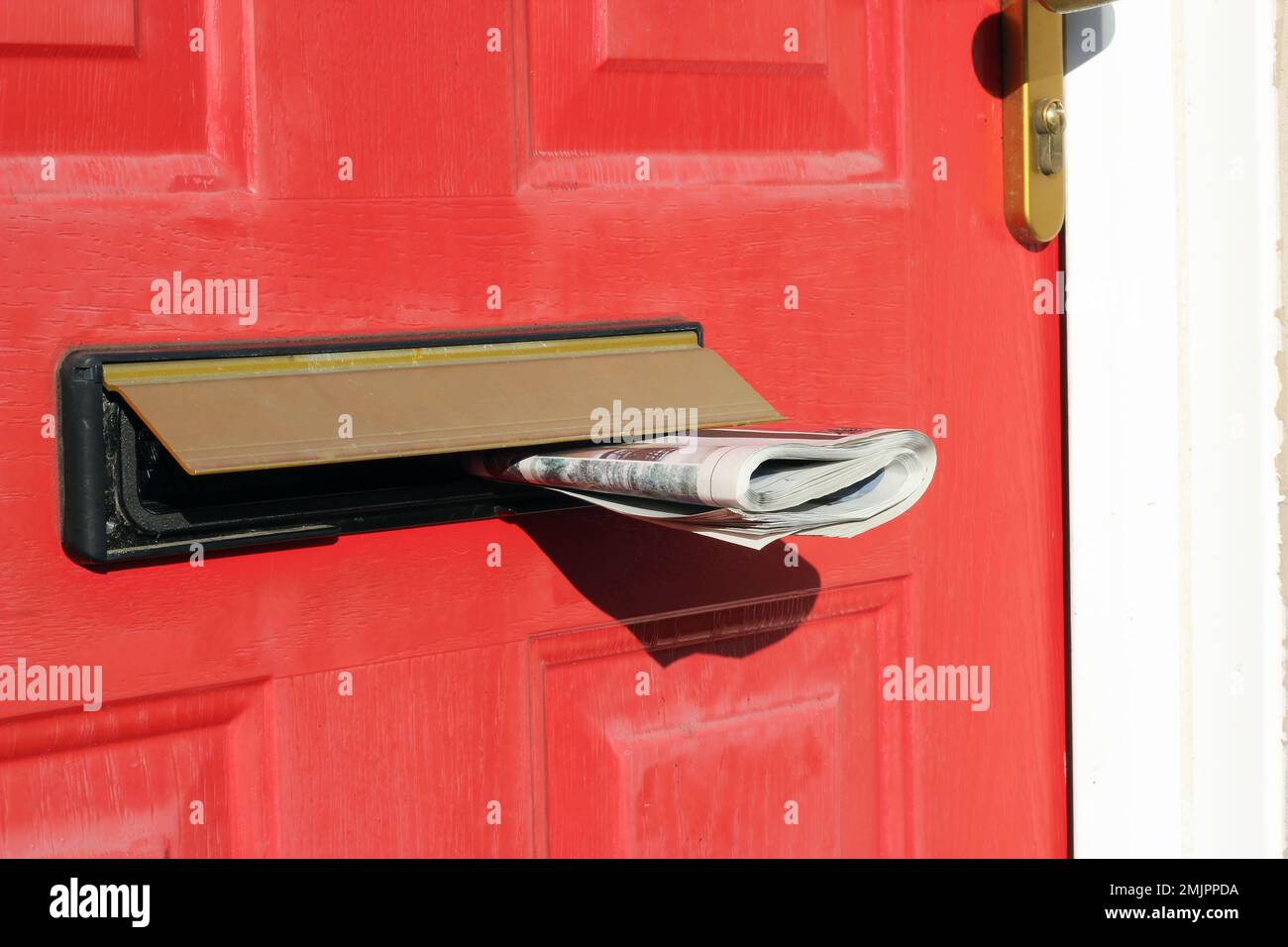 Close up of a letter box in a red front door with a newspaper sticking ...