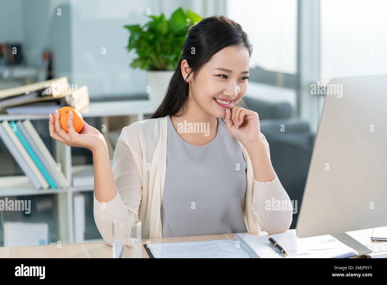 A young woman with an orange in the office Stock Photo - Alamy
