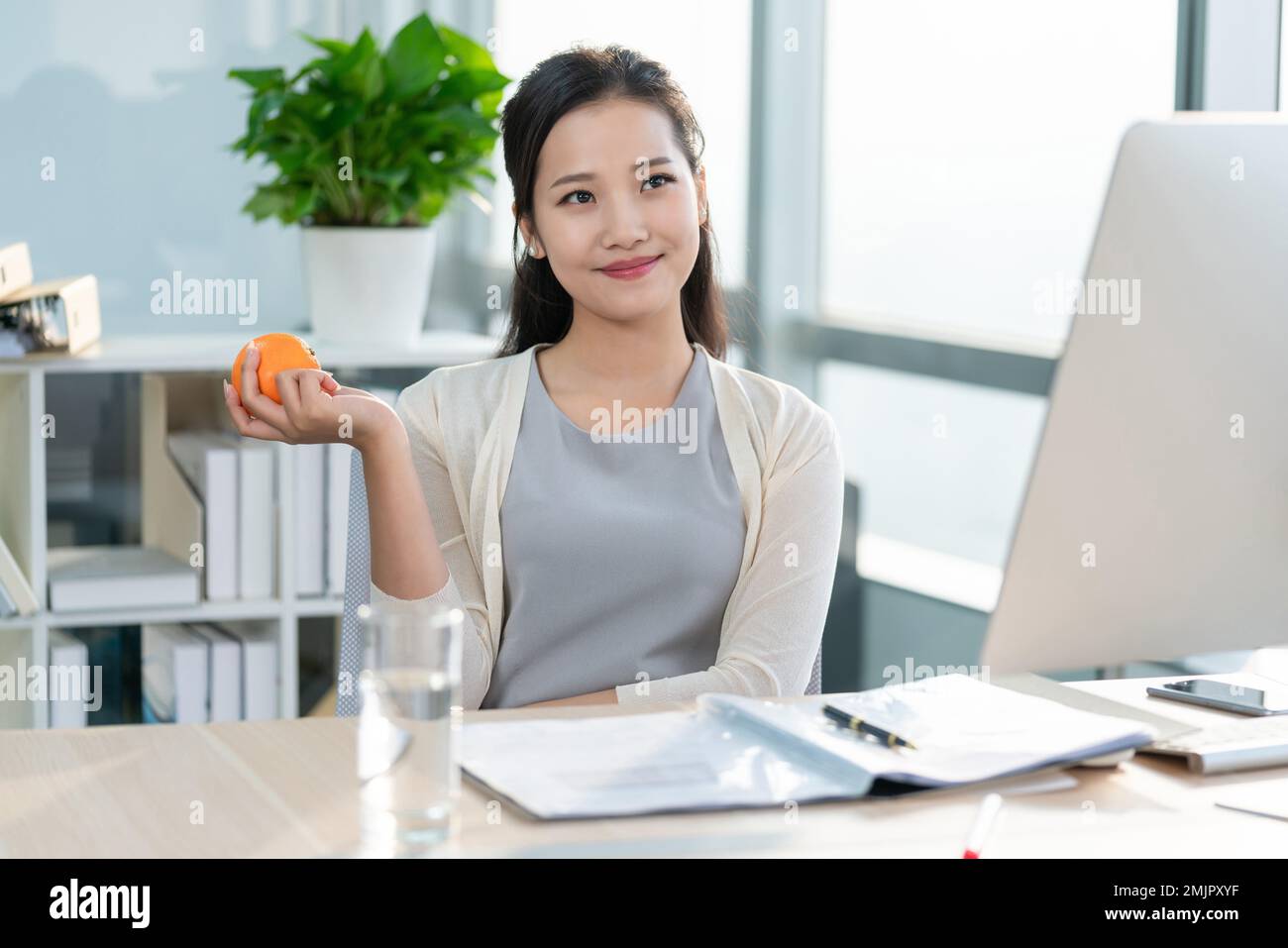 A young woman with an orange in the office Stock Photo - Alamy