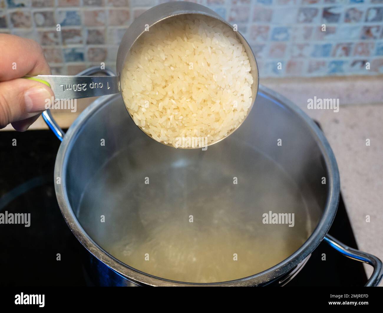 pouring rice from measuring cup into boiling water in saucepan on ...
