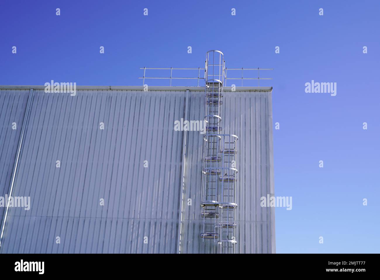 Ladder to the roof of a tall industrial building on blue sky background ...