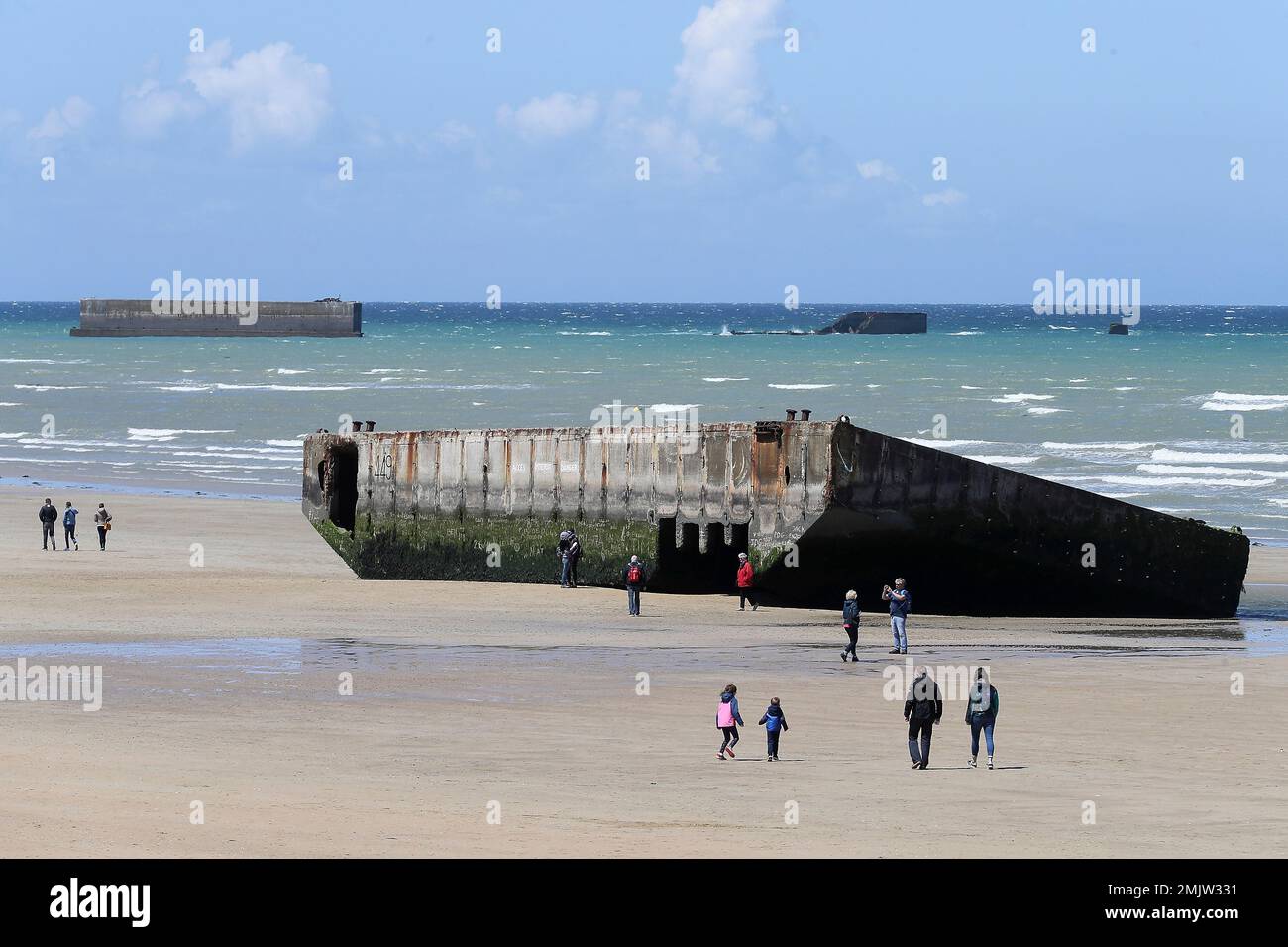Poeple walk by remains used for D-Day on the Arromanches beach, just ...