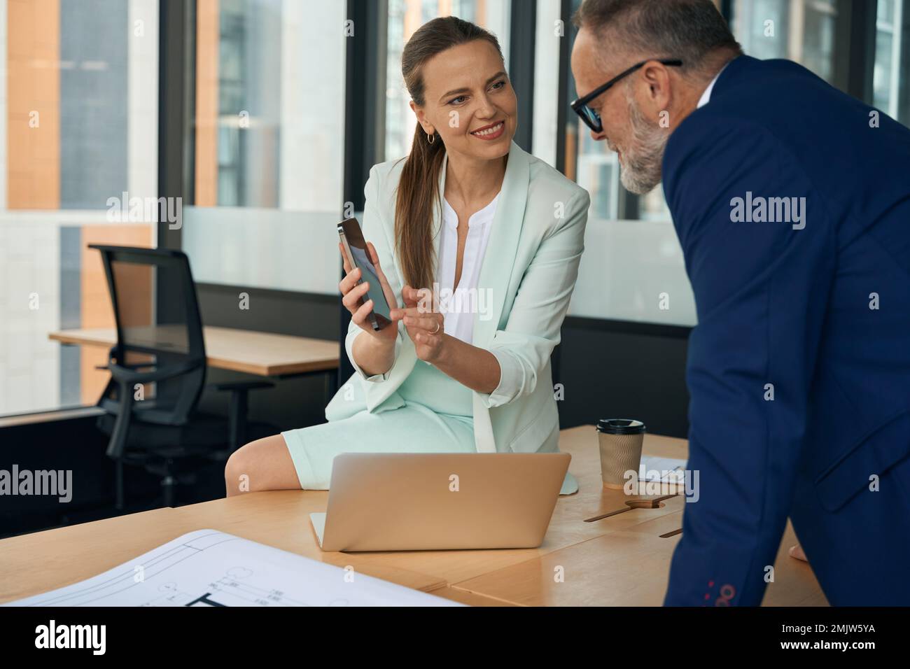 Merry woman in business suit showing phone screen to colleague Stock ...
