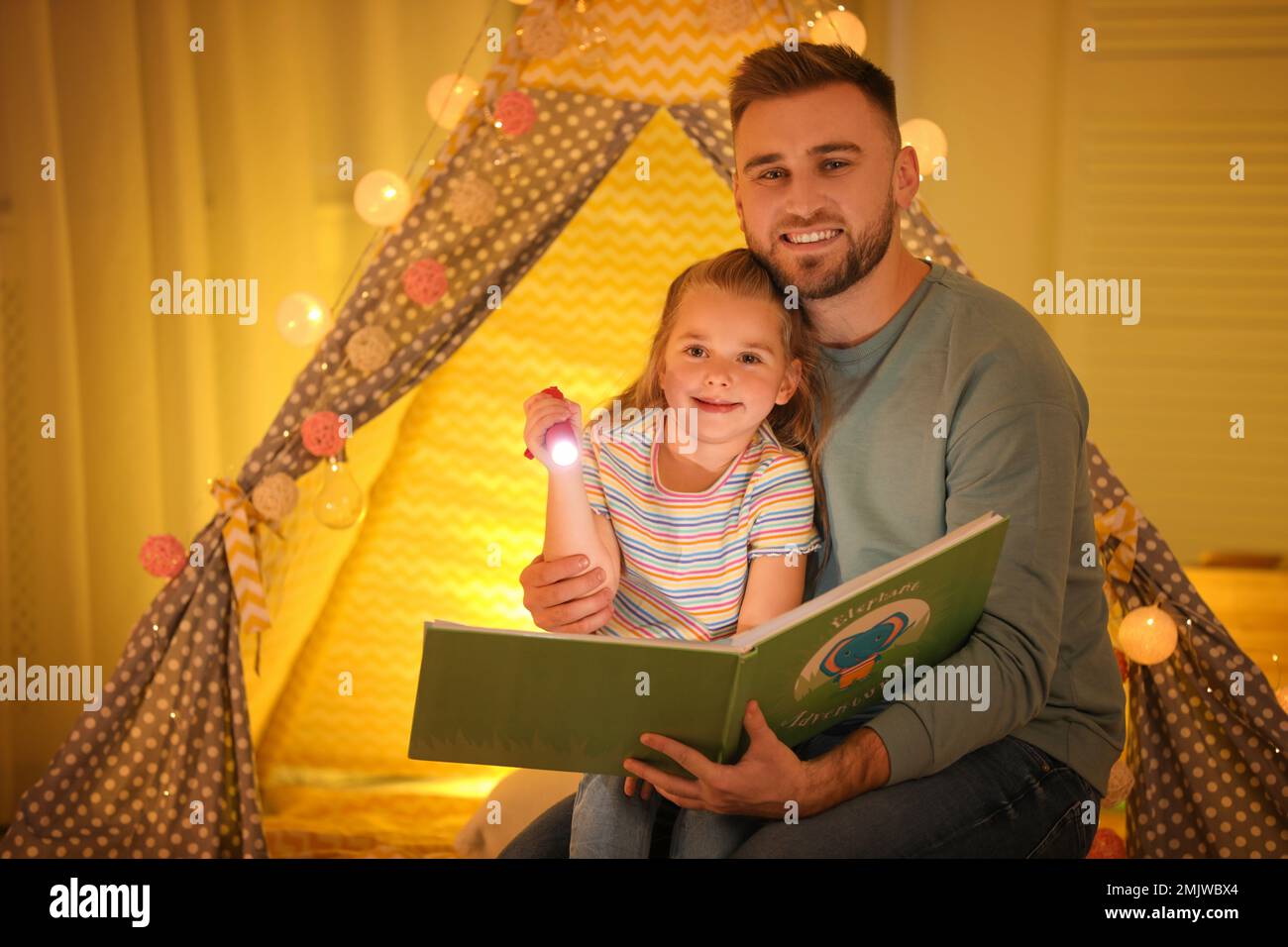 Father and daughter with flashlight reading book at home Stock Photo ...