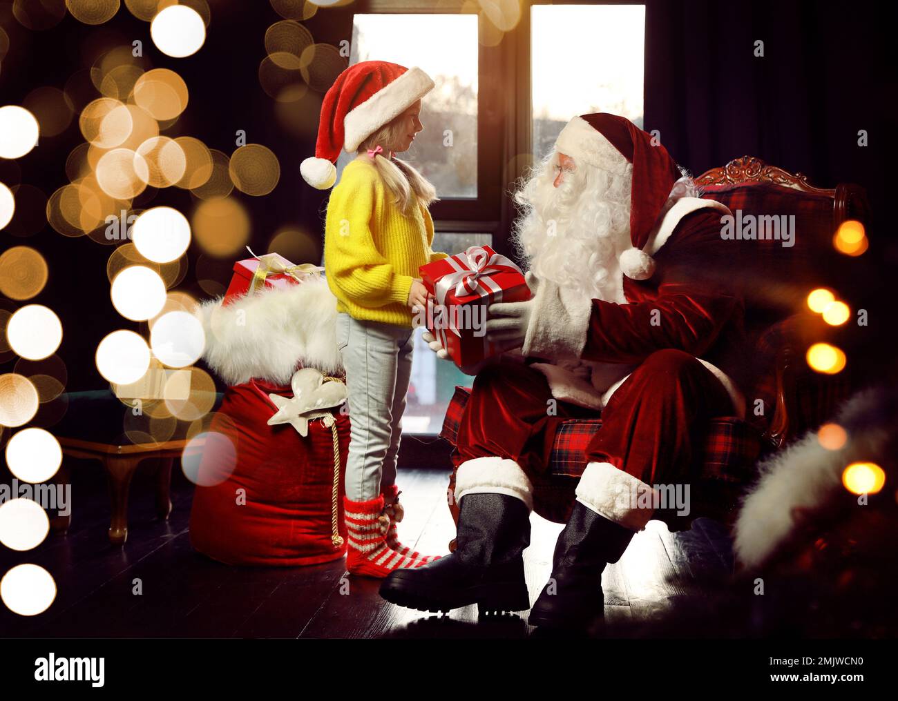 Santa Claus giving Christmas gift to little girl near window indoors ...