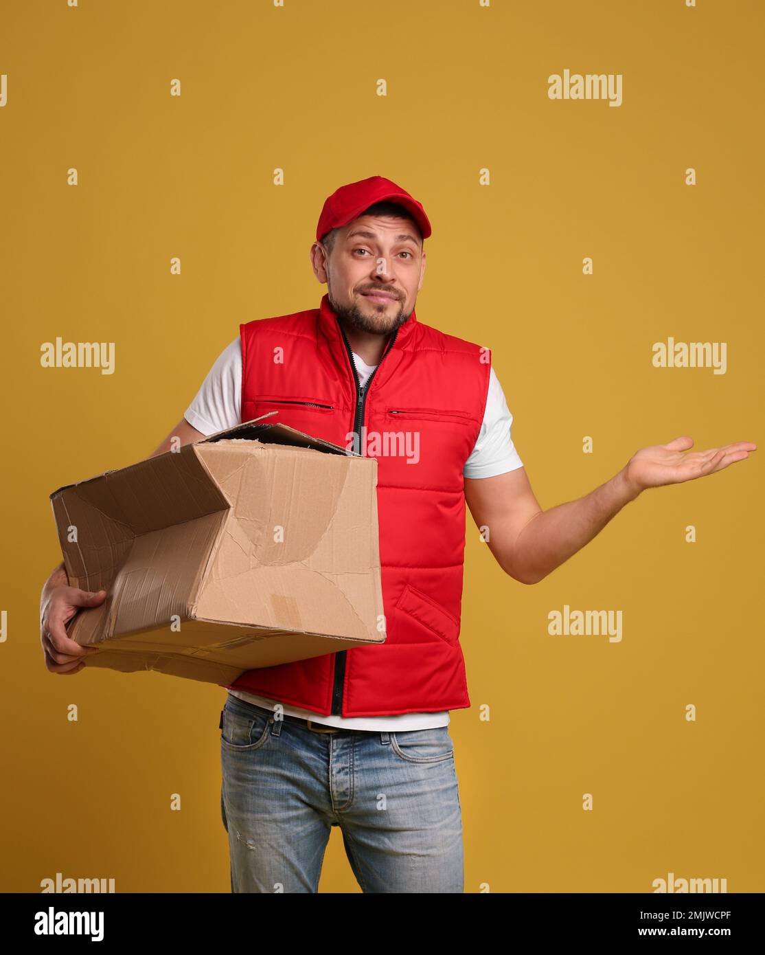 Emotional courier with damaged cardboard box on yellow background. Poor ...