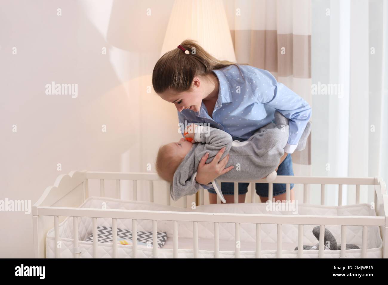 Teen nanny putting cute little baby in crib at home. Daytime sleep ...