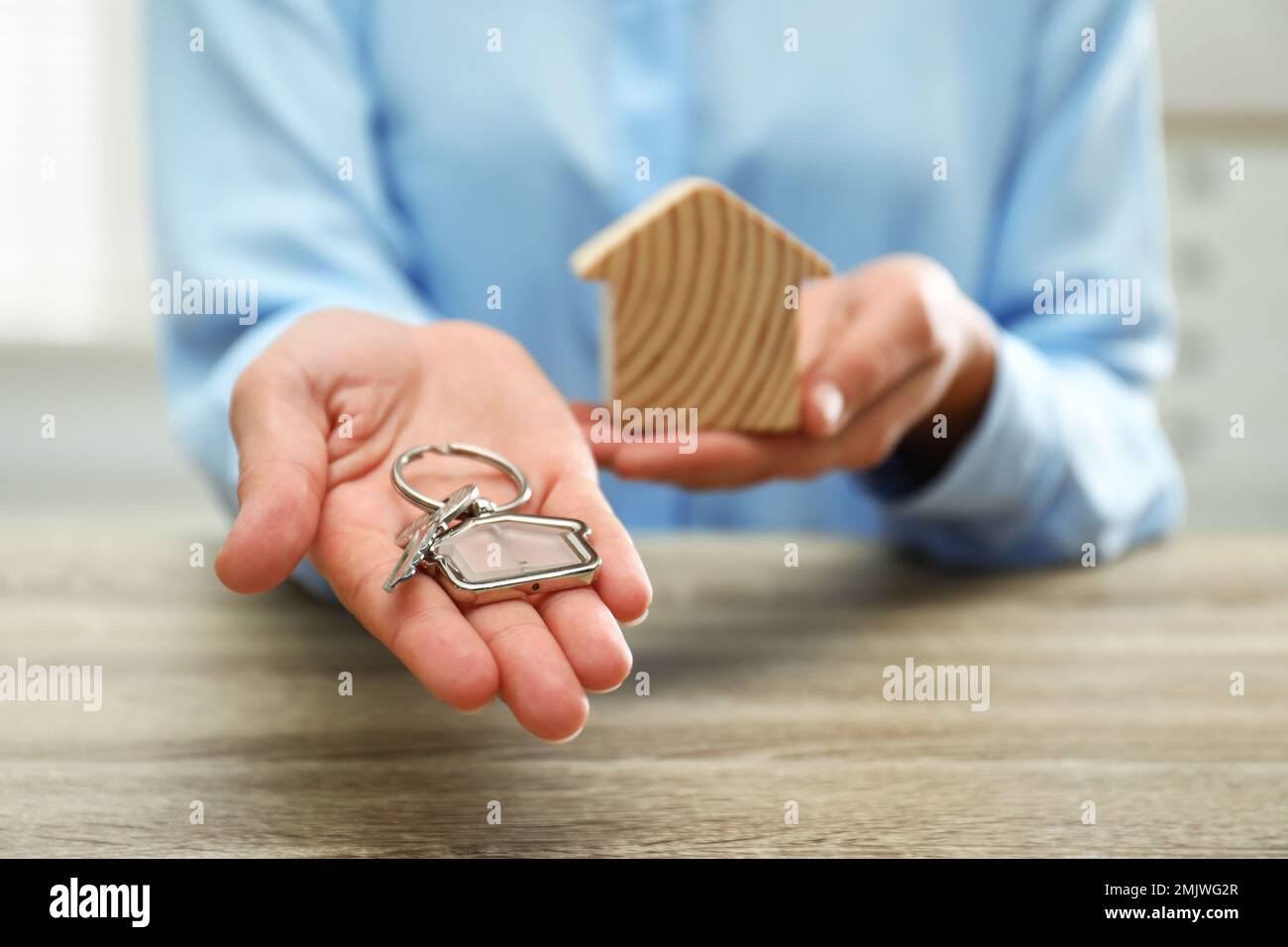 Real estate agent holding house figure and key at wooden table, closeup ...