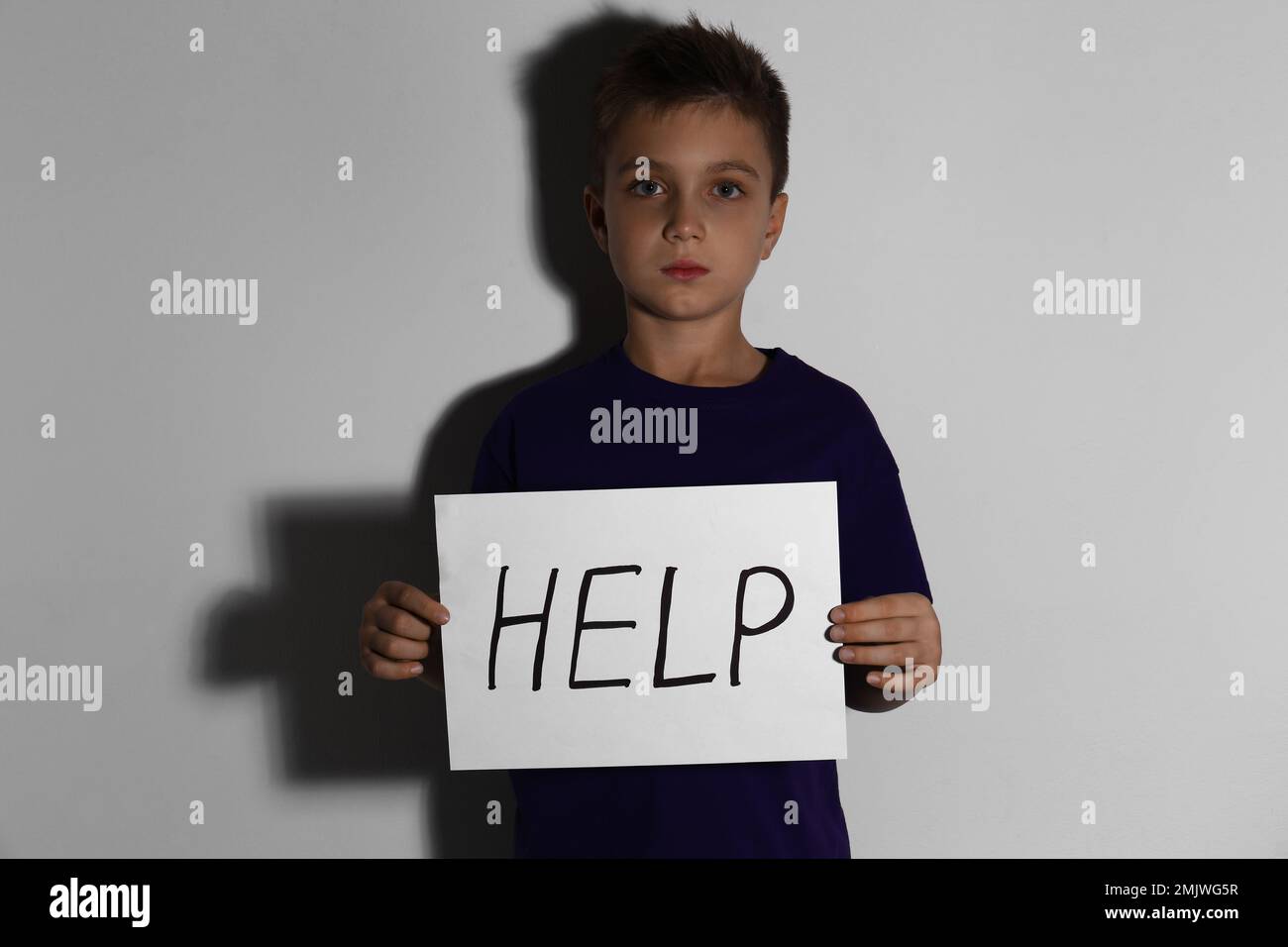Abused little boy with sign HELP near white wall. Domestic violence ...