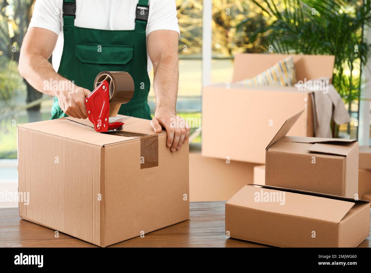 Man packing box with adhesive tape indoors, closeup. Moving service ...