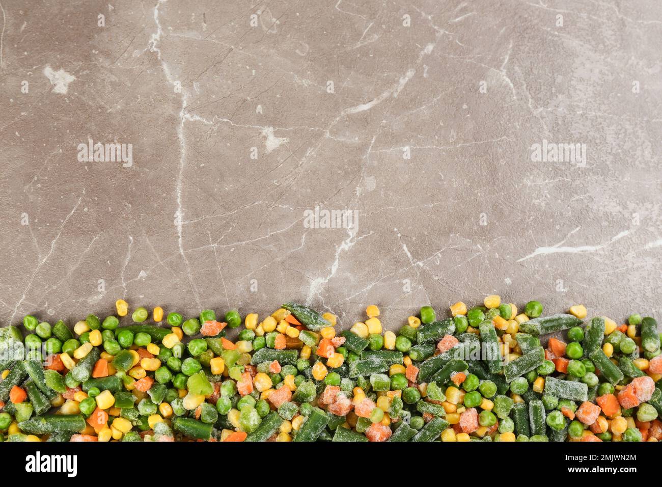 Frozen vegetable mix on brown marble table, top view. Space for text ...