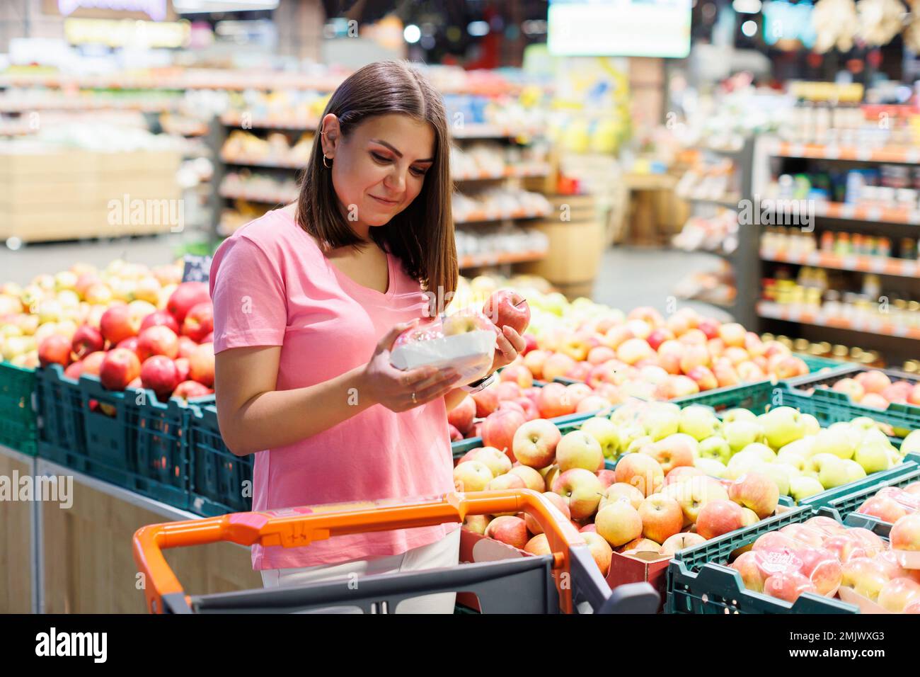 Young brunette woman picks chooses fruits on the counter in supermarket ...