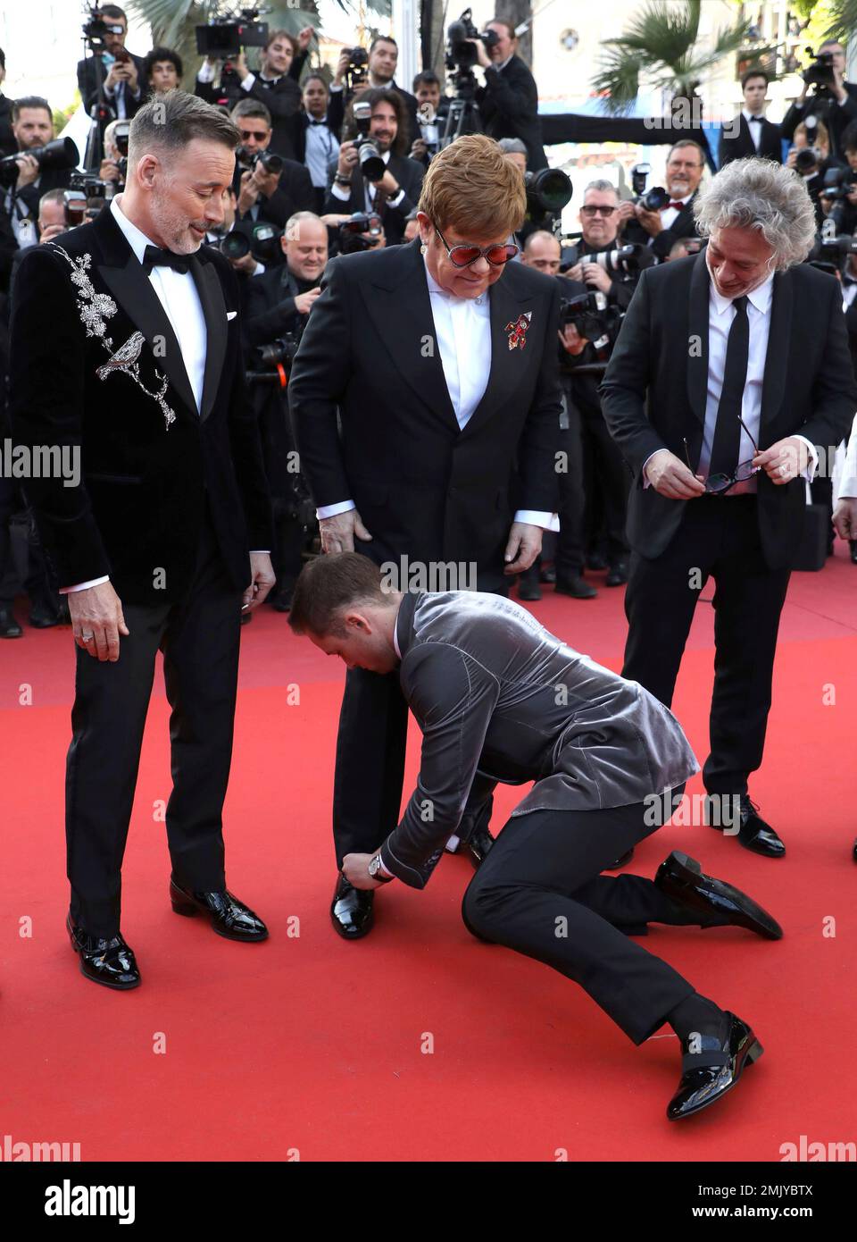 Actor Taron Egerton, center, ties the shoelaces of singer Elton John ...
