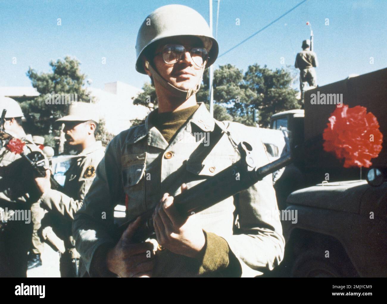 An Iranian soldier poses with a rose in the barrel of his rifle as he ...