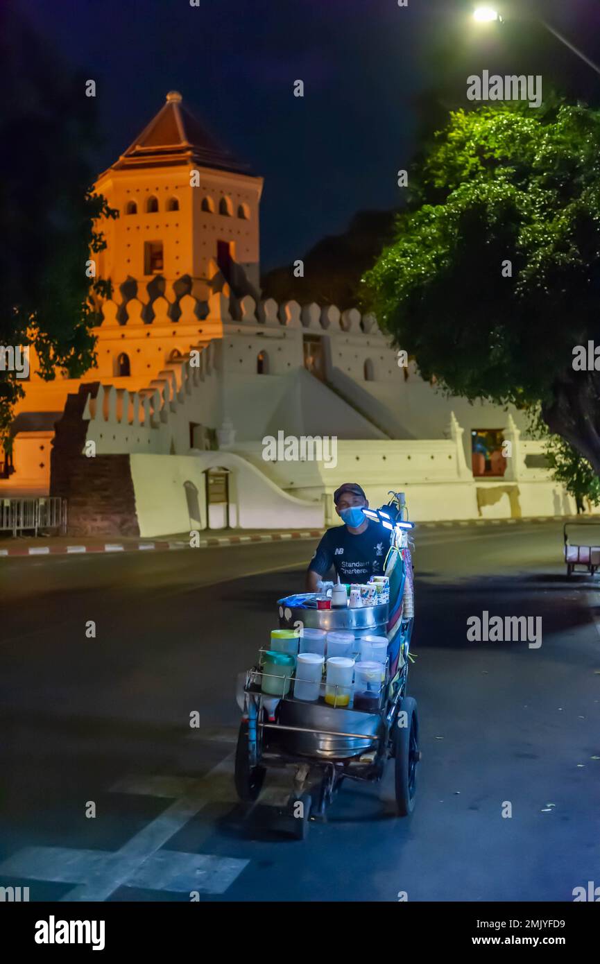 A street food vendor walking down the Phra Athit Road at night, with ...