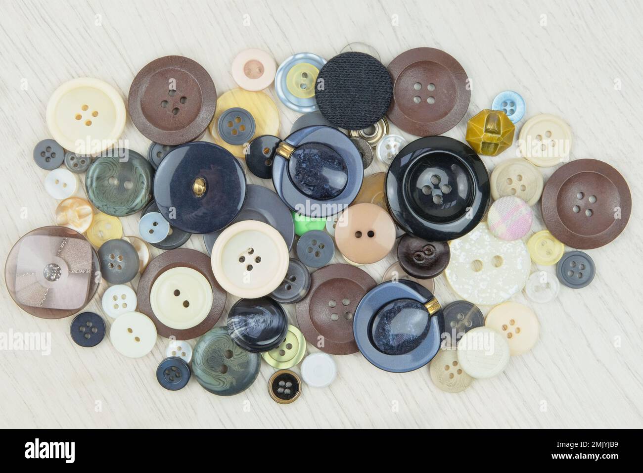 Variety of buttons of different colors and sizes on a light wooden ...
