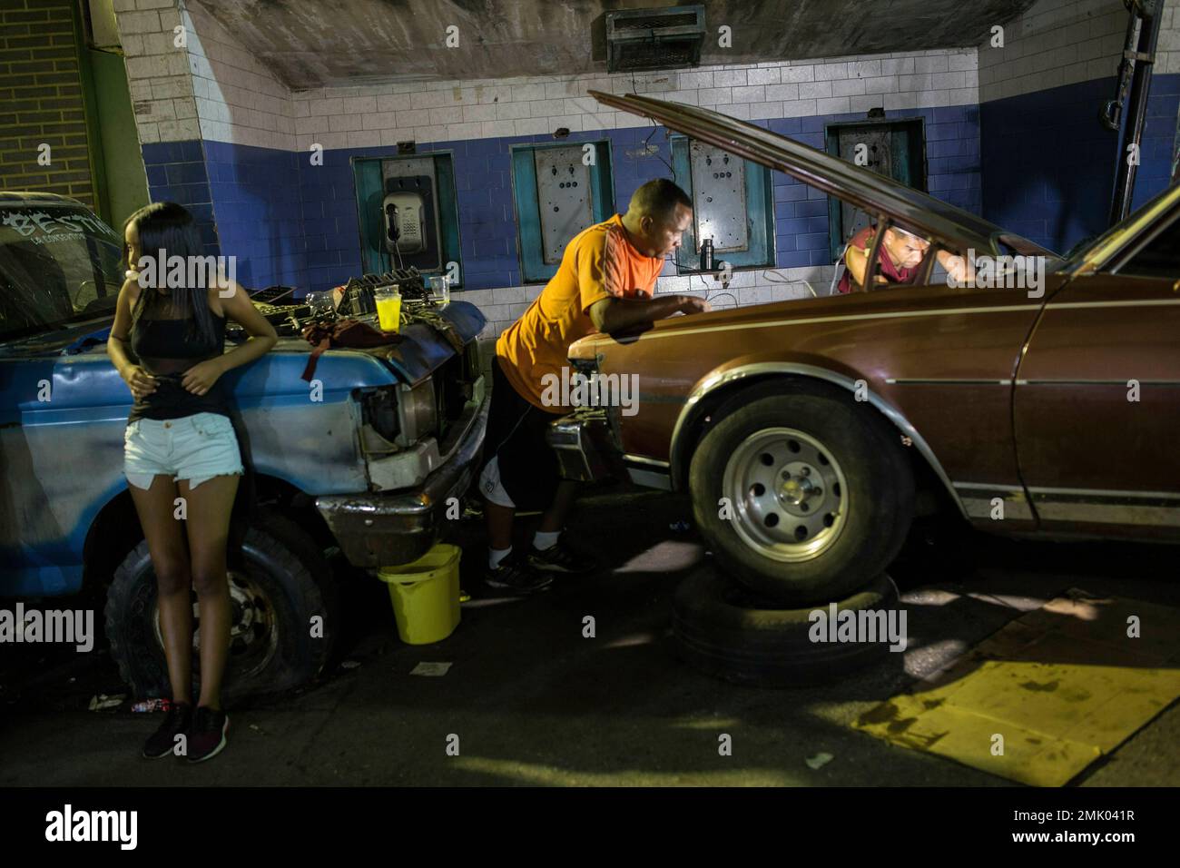 Men spend the evening repairing a car outside their home as a young ...