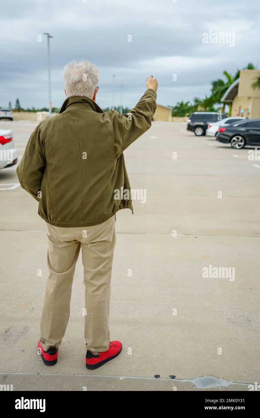 Old man looking for his car in a parking lot by pushing the unlock ...